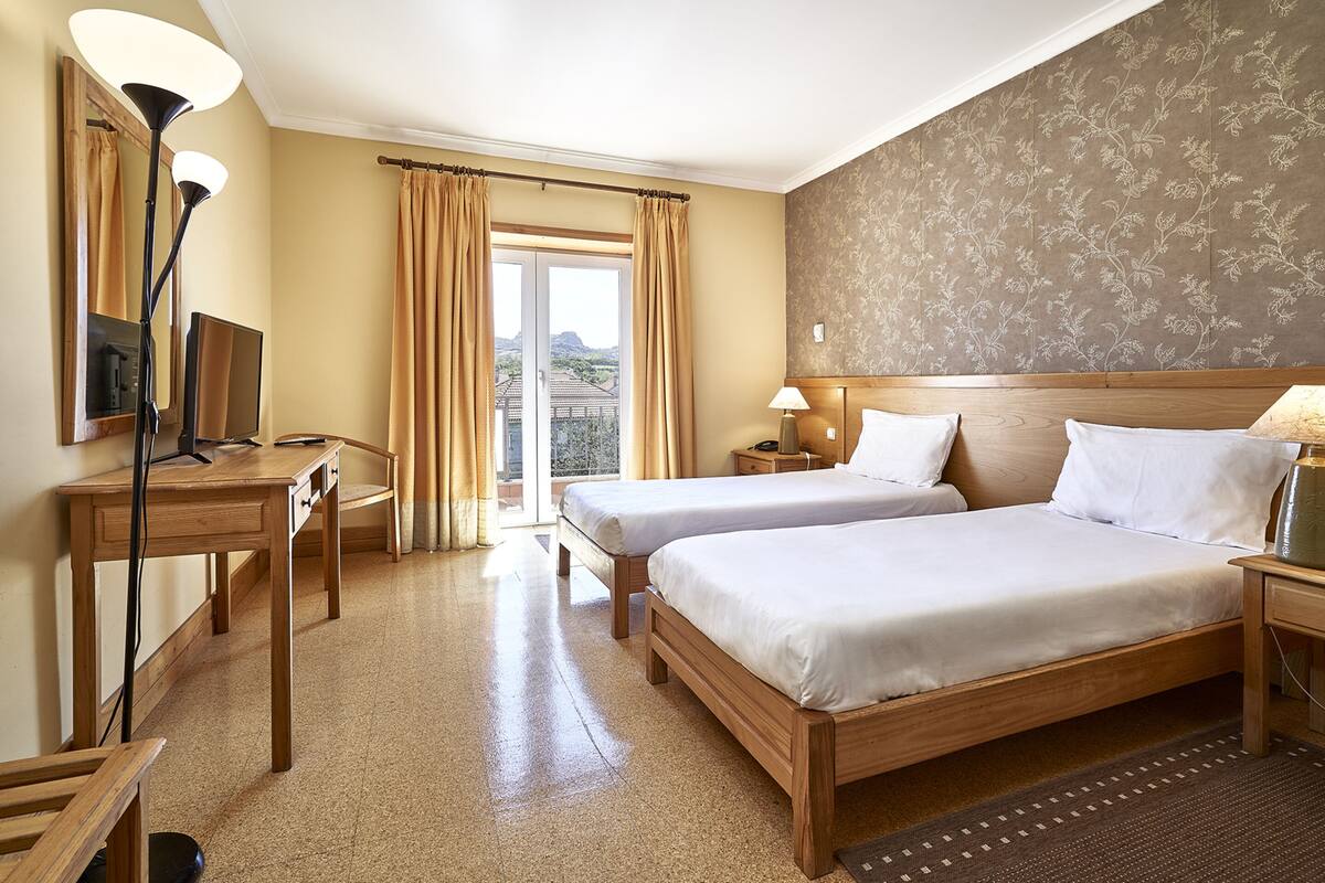 Quarto de hotel com duas camas, uma escrivaninha, televisão e vista para o exterior.