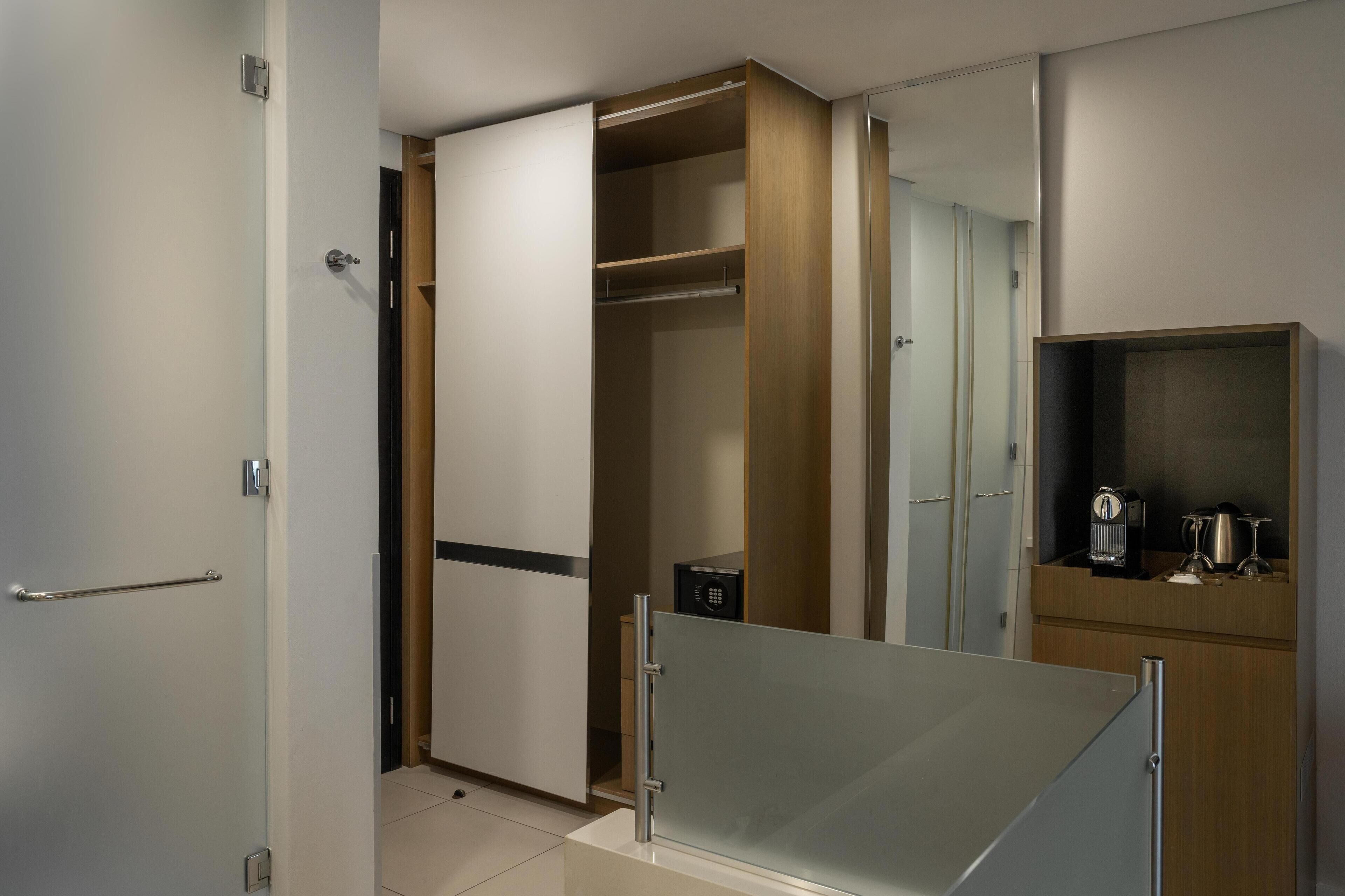 Quarto de hotel moderno com closet espaçoso, minibar e um espelho grande.