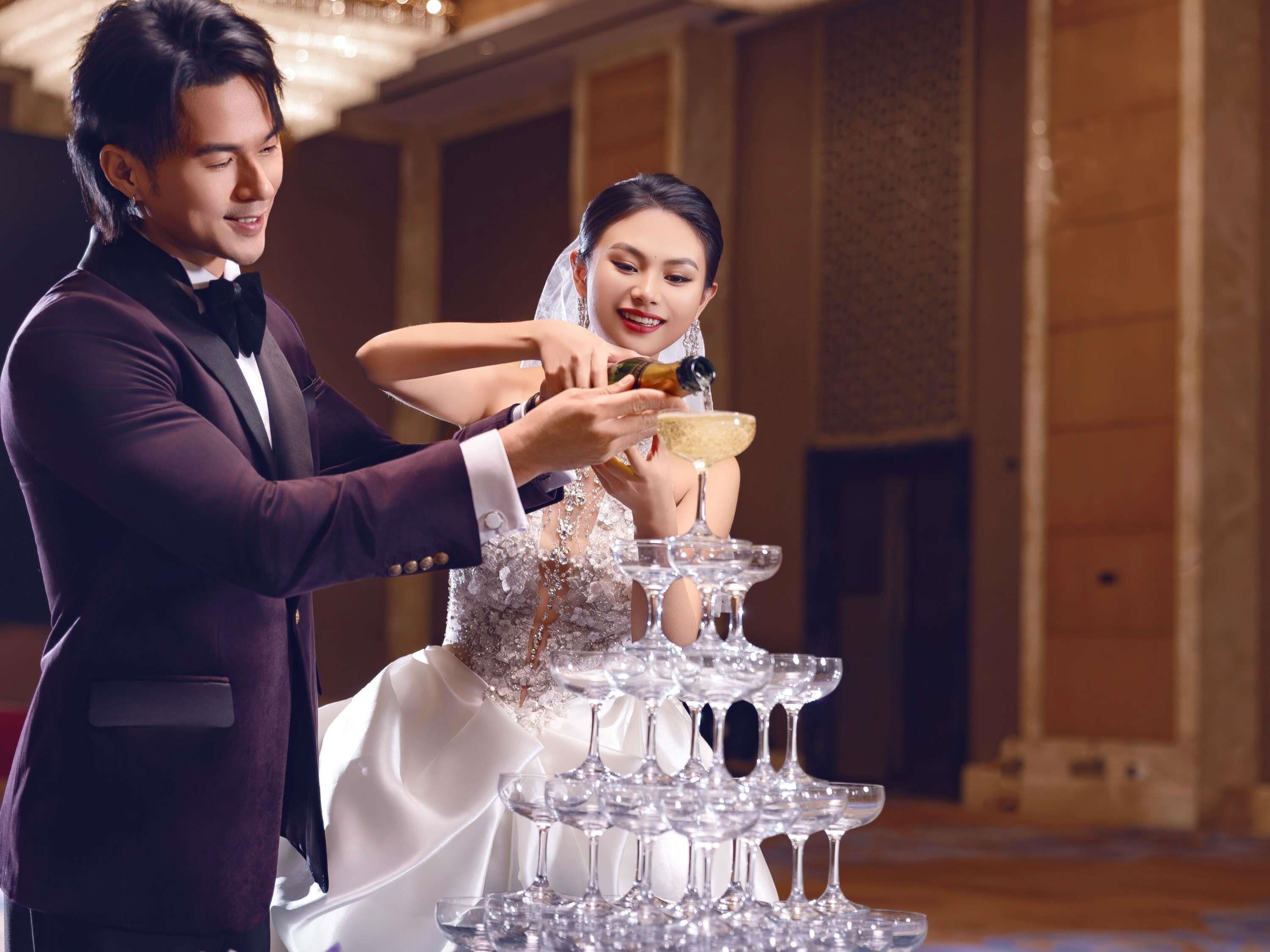 Um casal à mesa com uma vitrine de vidro em vários níveis, possivelmente para uma recepção de casamento.