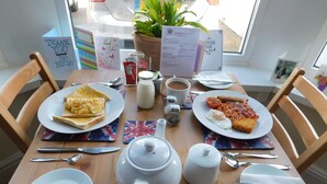 Uma mesa de café da manhã com pratos de ovos, torradas e feijão, um bule, saleiro e pimenteiro, e um cardápio.