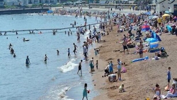 Uma praia movimentada com pessoas nadando e caminhando pela orla.