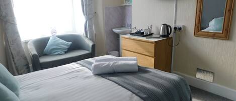 Quarto de hotel com cama, poltrona, escrivaninha com pia, televisão e janela com cortinas.