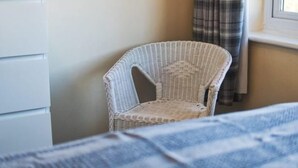 Uma cadeira de vime em um quarto com cômoda branca e uma janela com cortinas.