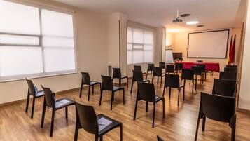 Uma sala de conferências com fileiras de cadeiras, uma tela de projetor e uma mesa vermelha.
