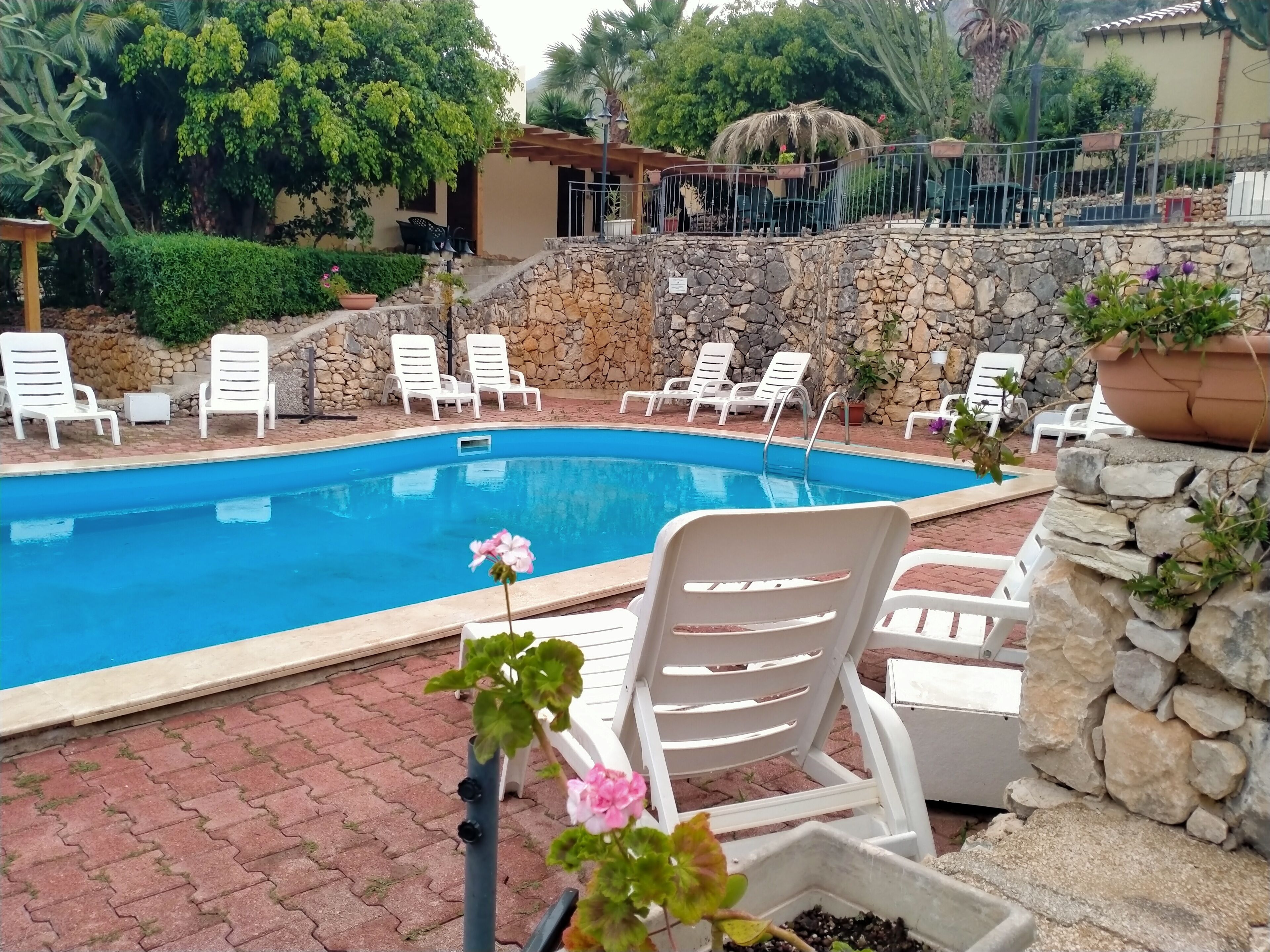 Piscina com cadeiras de descanso brancas e parede de pedra.