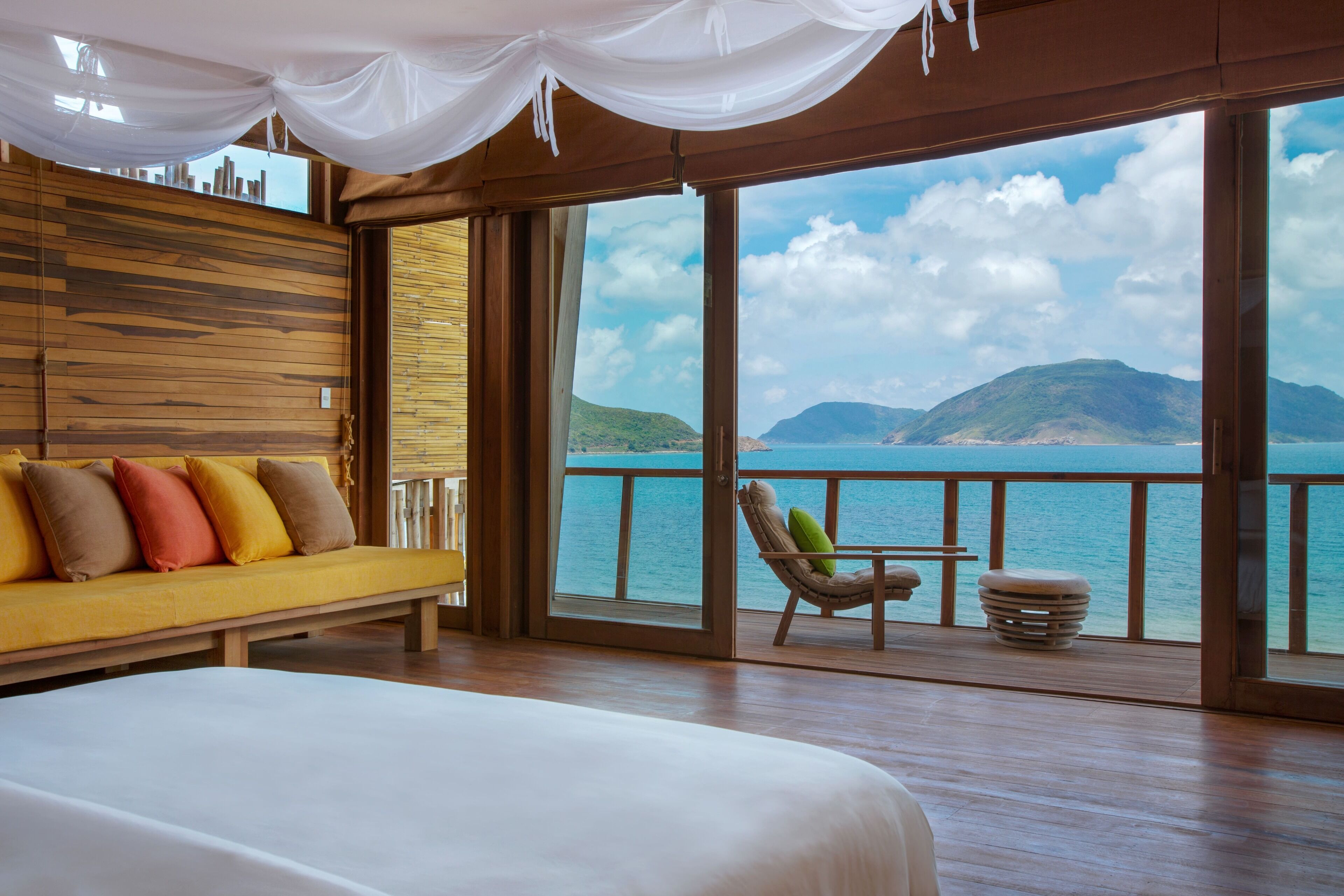 Quarto com uma cama grande, um sofá e uma cadeira, com vista para o mar e as montanhas.