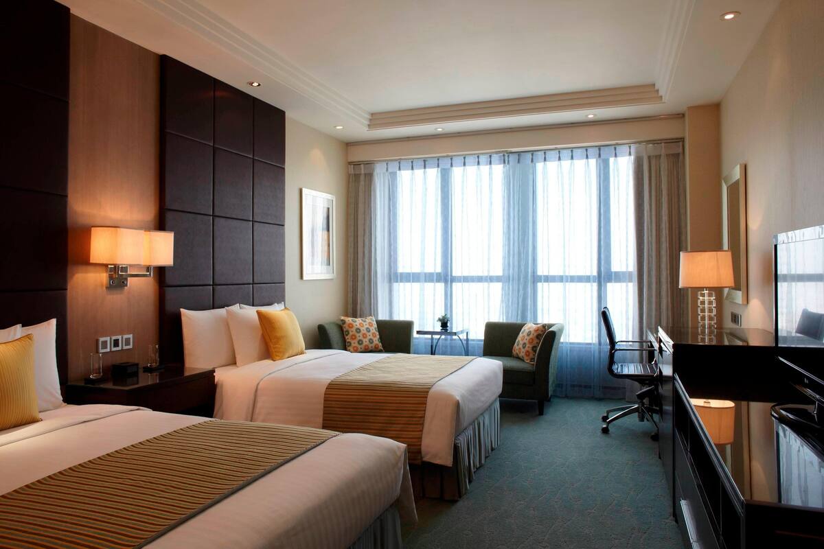 Quarto de hotel com duas camas, uma mesa, uma cadeira e uma televisão.