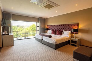 Quarto de hotel com uma cama grande, televisão, escrivaninha e varanda com vista para áreas verdes.