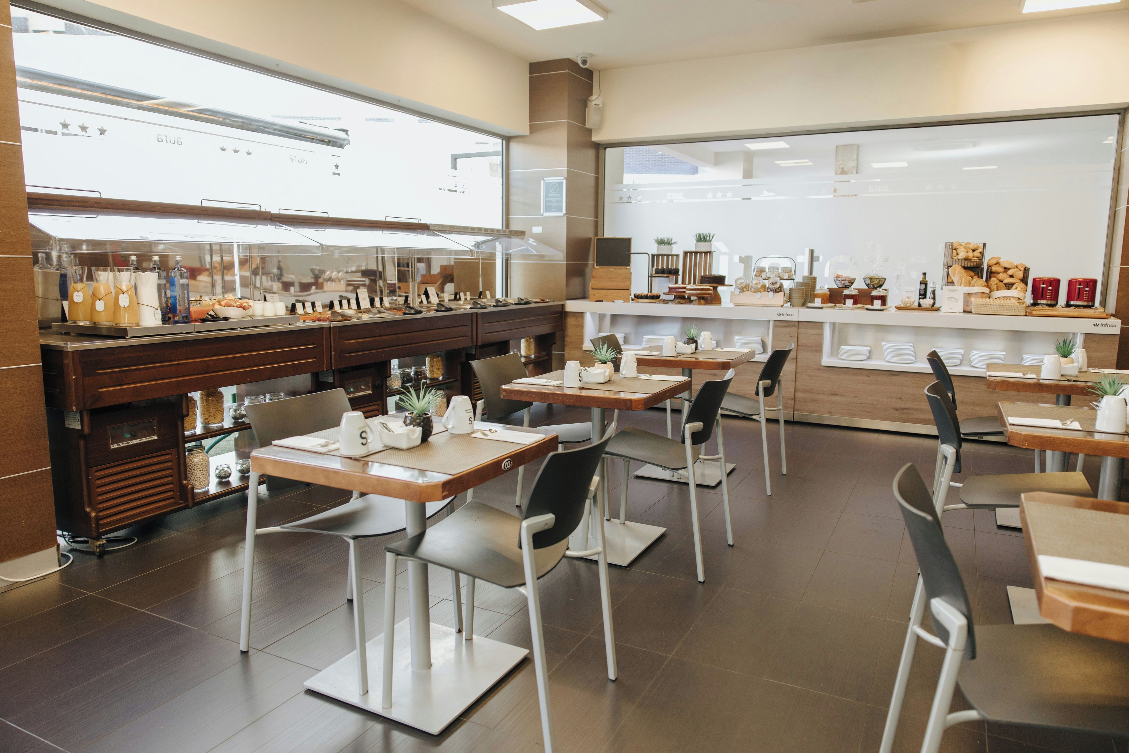 Um café com mesas, cadeiras, balcão de buffet e um quadro branco na parede.