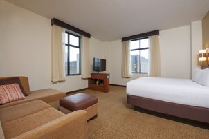 Quarto de hotel com cama, sofá, televisão e um pequeno armário.