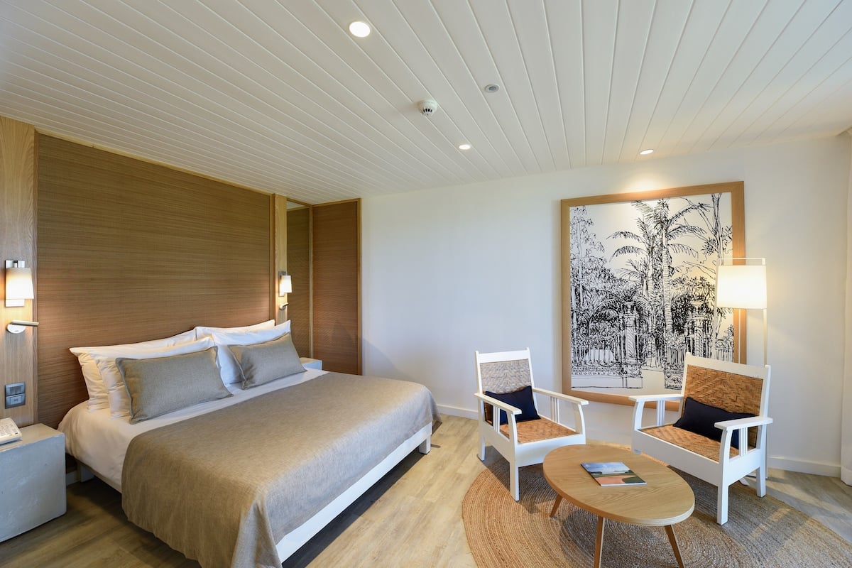 Quarto de hotel com cama, duas cadeiras, uma mesa e uma grande obra de arte na parede.