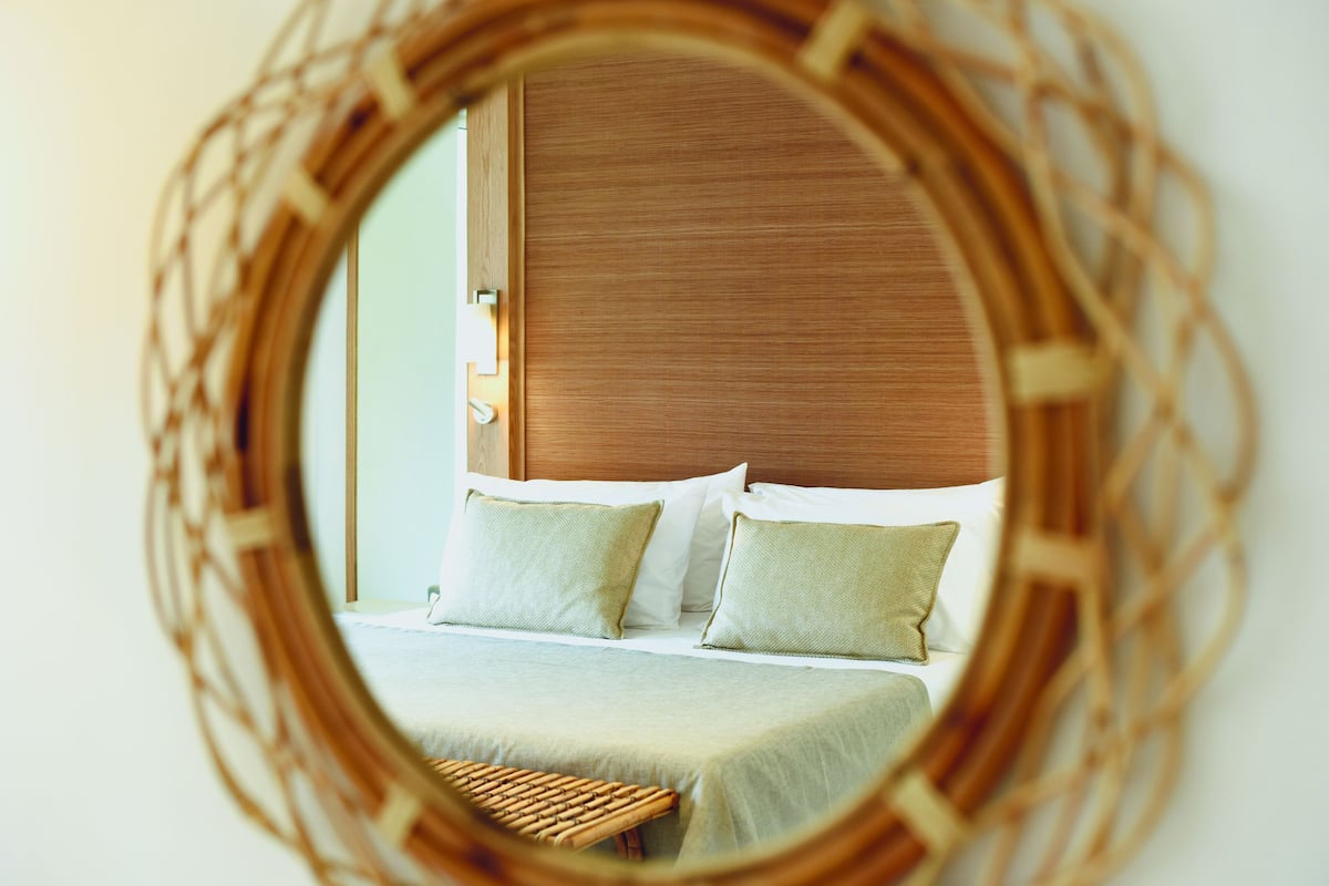 Uma cama com cabeceira de madeira, duas almofadas e um cesto de palha no rodapé da cama.