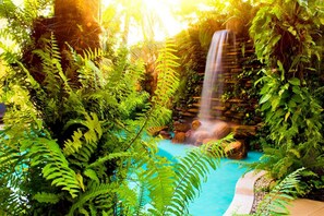 Um jardim exuberante com uma cascata, uma piscina e vegetação densa.