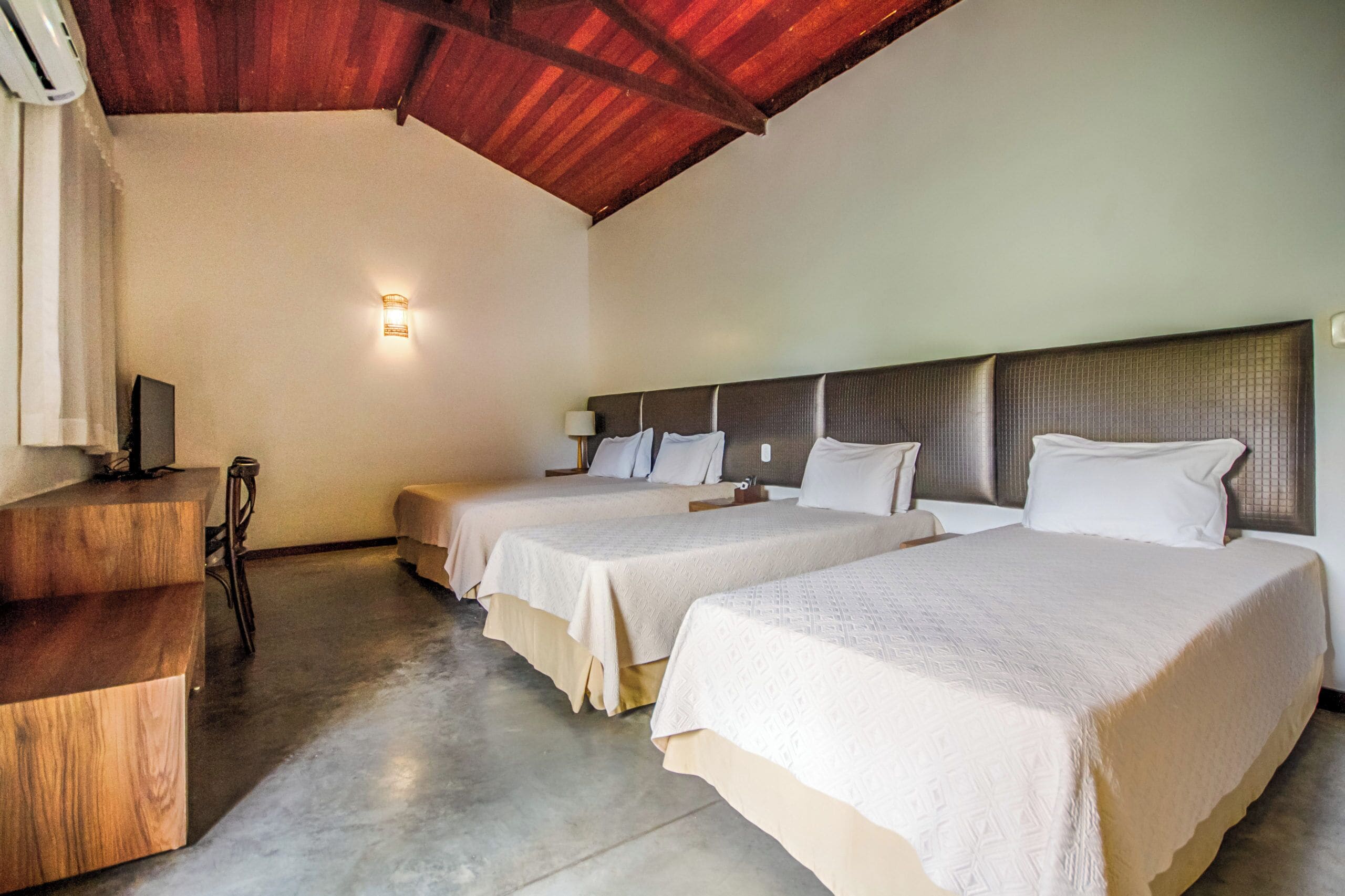 Quarto de hotel com duas camas, uma escrivaninha de madeira e um ventilador de teto.