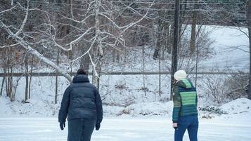 Duas pessoas patinam no gelo sobre um caminho coberto de neve em uma área arborizada.