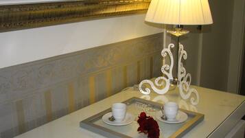 Uma mesa com bandeja que segura duas xícaras, um objeto decorativo, um abajur e um quadro na parede.