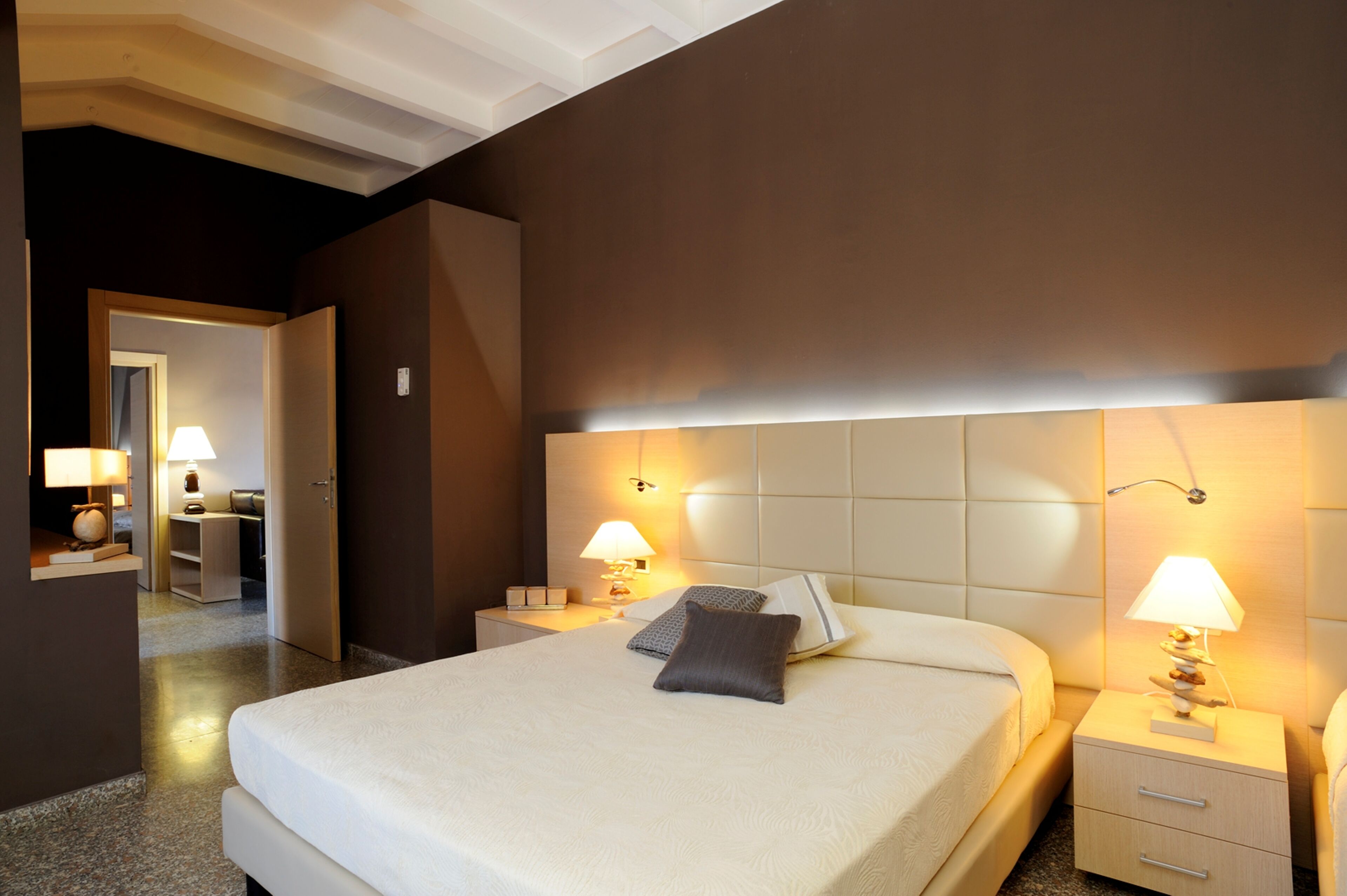 Quarto de hotel com uma cama grande, duas mesas de cabeceira com abajures, um espelho e uma porta para o banheiro.