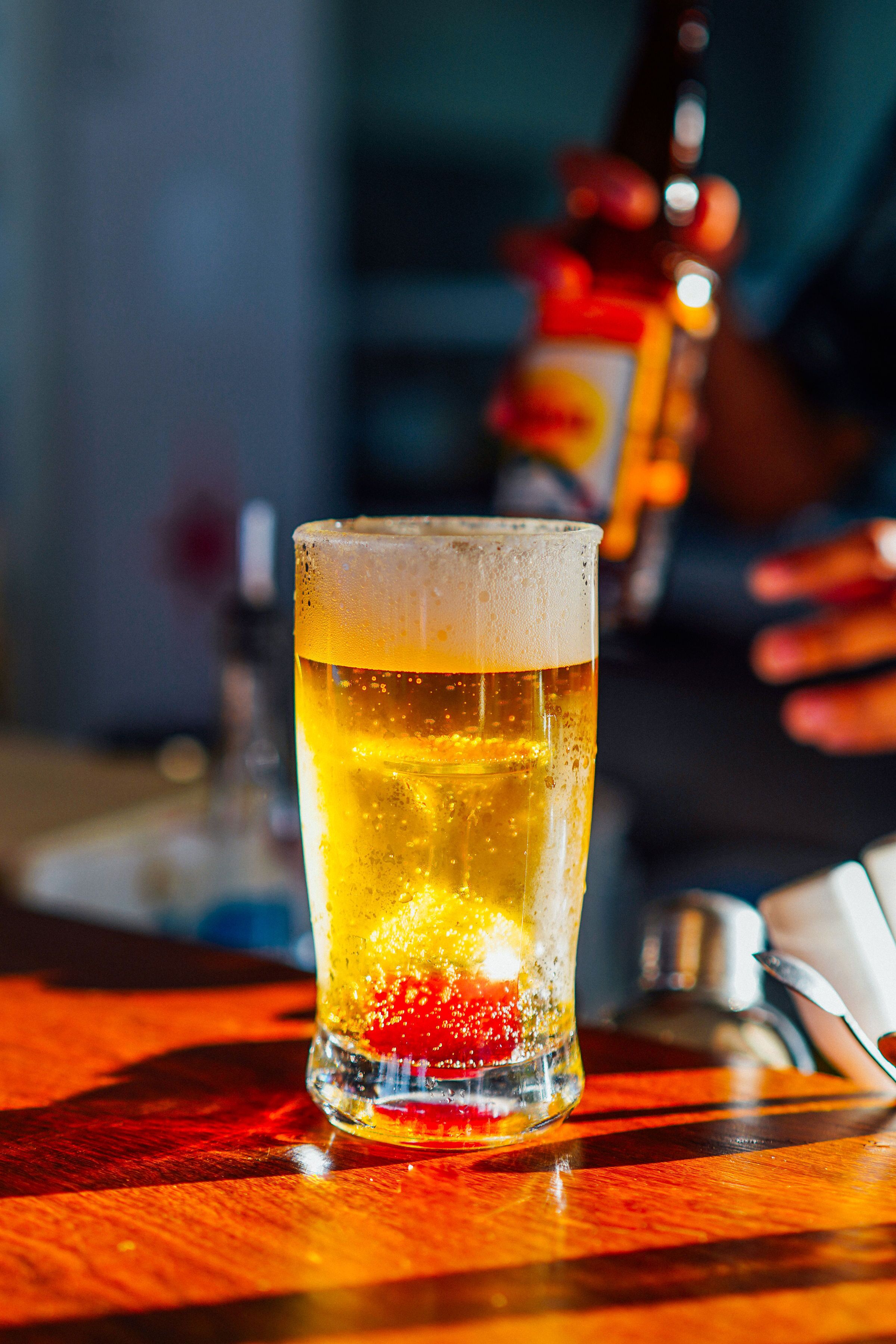 Um copo de cerveja com espuma em um balcão de madeira.