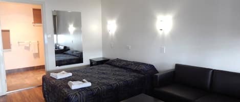 Quarto de hotel com cama, sofá, mesa pequena e espelho.