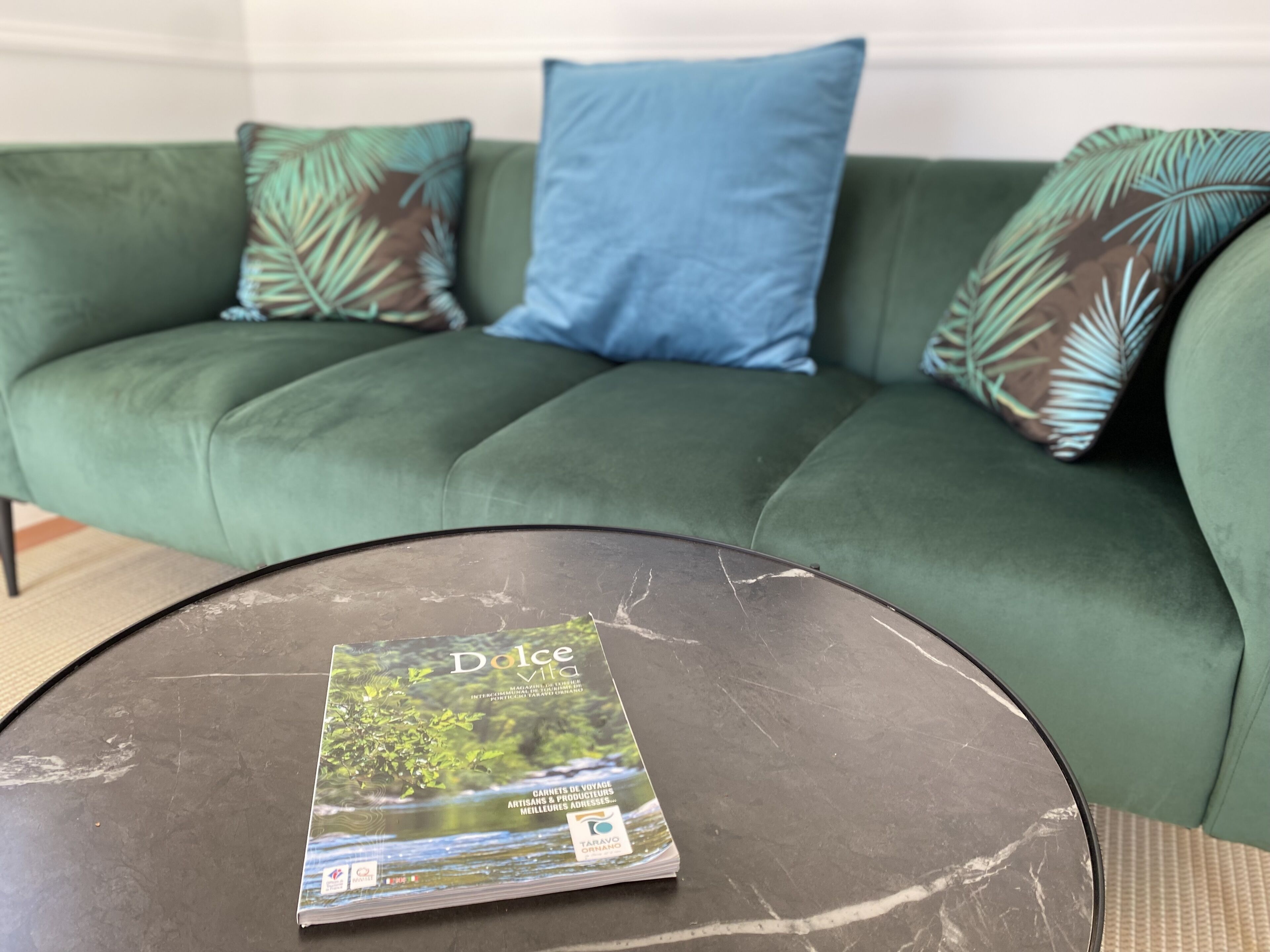 Um sofá verde com almofadas estampadas e uma revista sobre uma mesa redonda.
