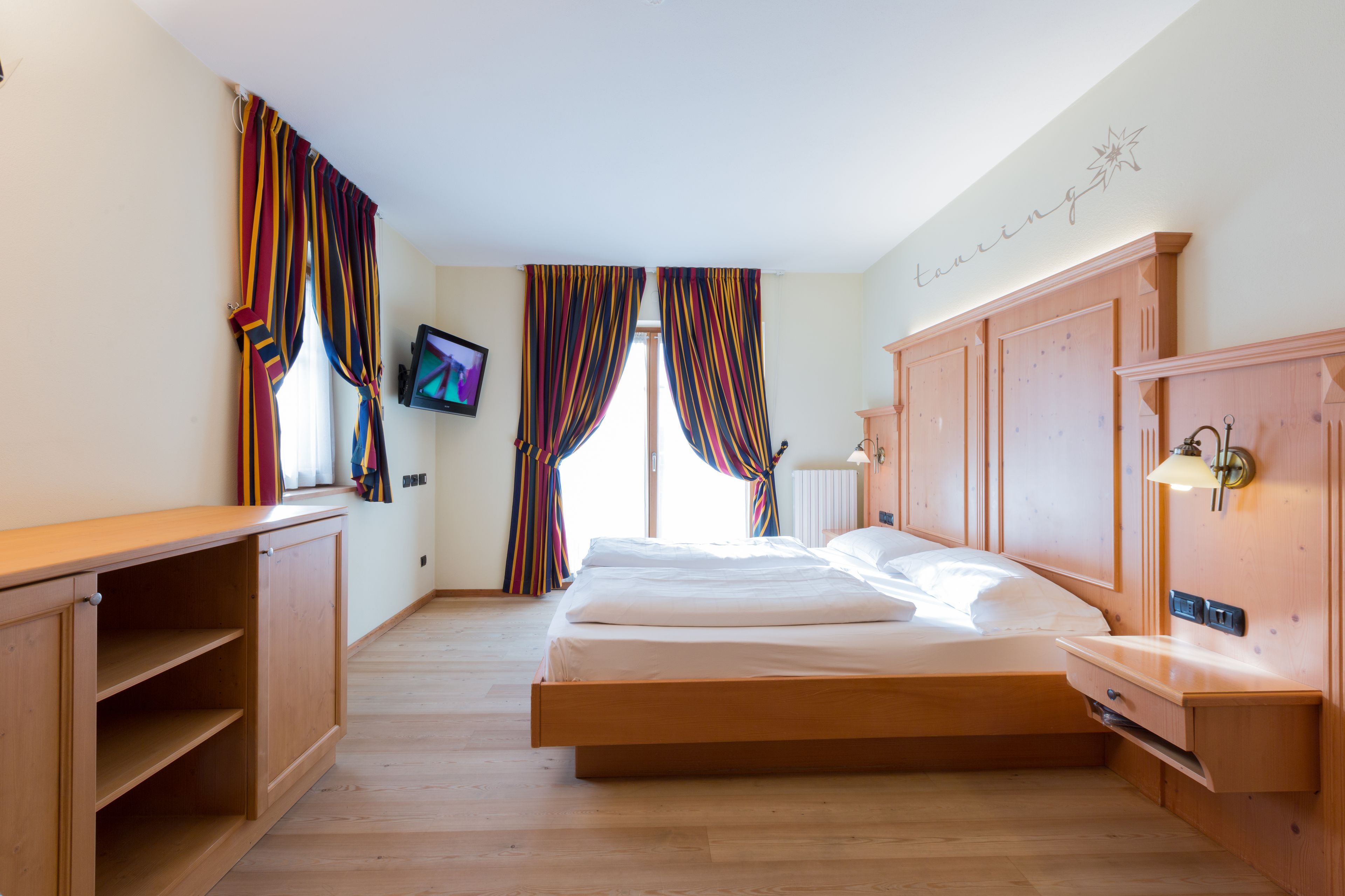 Quarto com cama de madeira, televisão na parede e cortinas coloridas.