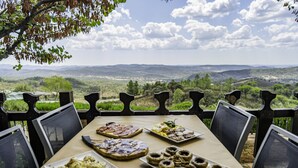 Uma mesa posta para refeição com diversos pratos, com vista para uma paisagem panorâmica.
