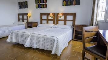 Quarto de hotel com duas camas, cabeceira de madeira, mesa de cabeceira, uma cadeira e uma janela com cortinas.