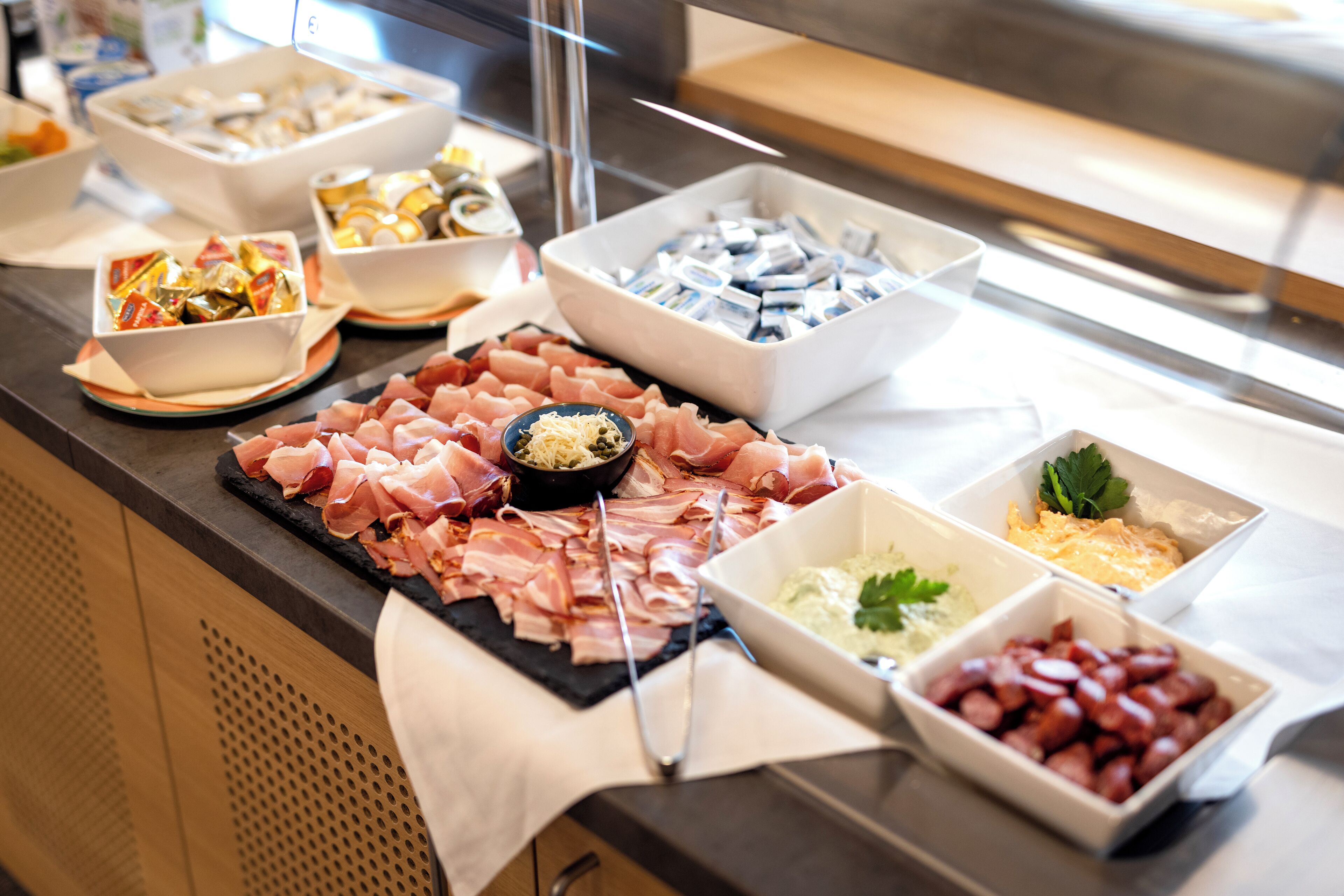 Buffet com diversos alimentos, incluindo carnes, queijos e acompanhamentos.