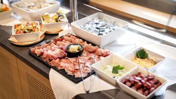 Buffet com diversos alimentos, incluindo carnes, queijos e acompanhamentos.