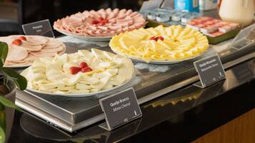 Buffet com diversos alimentos, incluindo uma travessa de queijo fatiado e uma travessa de frutas.