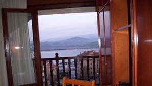 Uma varanda com cadeira de madeira, vista para um corpo d'água e montanhas ao longe.