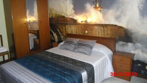 Quarto com cama, mesas de cabeceira, guarda-roupa e um mural de uma onda quebrando contra um farol.