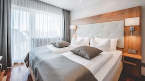 Quarto de hotel moderno com uma cama grande, duas mesas de cabeceira, um painel de cama de madeira e uma janela ampla com cortinas.