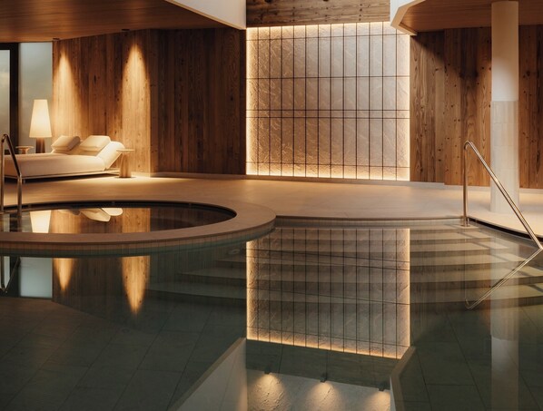 Uma área interna de piscina moderna, com parede de madeira e um espaço de estar com uma luminária.