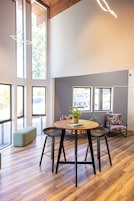 Uma área de refeições moderna com uma mesa redonda, quatro cadeiras e um banco. Janelas amplas proporcionam luz natural e vista para o exterior.