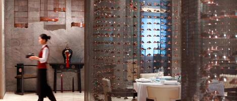 Interior de restaurante com design moderno, apresentando uma área de jantar com mesas preparadas para o serviço, um balcão de bar e gaiolas decorativas na parede.
