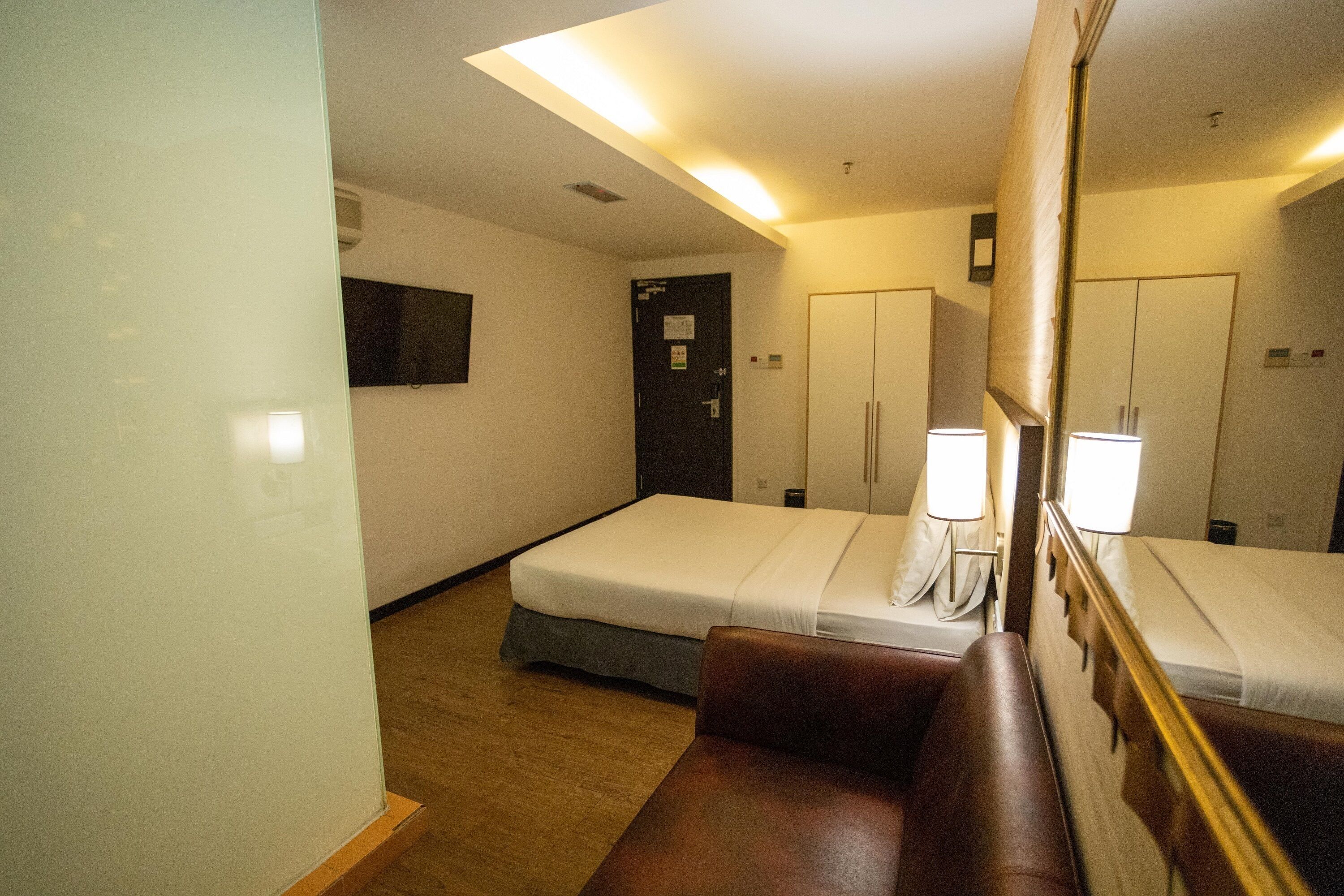 Quarto de hotel com uma cama de solteiro, um sofá, um guarda-roupa e uma televisão.
