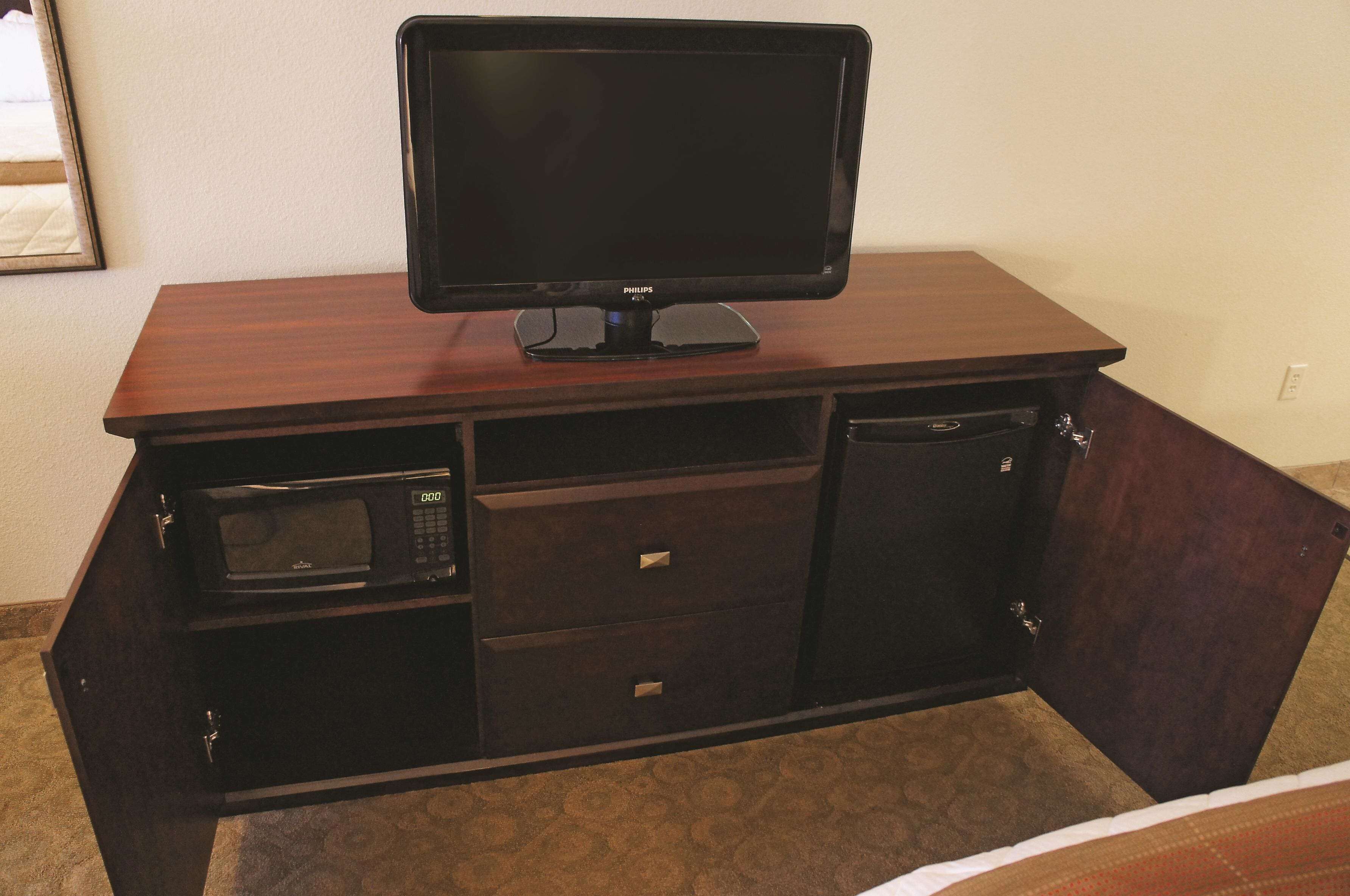 Um suporte de madeira para televisão com uma TV de tela plana, micro-ondas e uma pequena geladeira.
