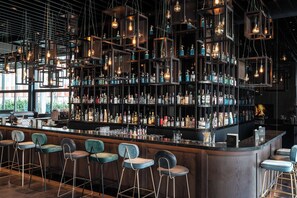 Uma área de bar com várias prateleiras de garrafas de bebidas, luminárias pendentes e banquetas.