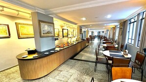 Um saguão de hotel com um balcão de buffet, mesas e cadeiras.