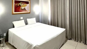 Quarto de hotel com uma cama grande, cortinas cinzas e um quadro na parede.