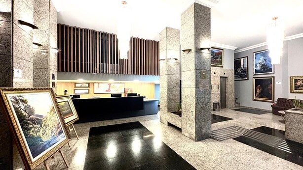 Um saguão com balcão de atendimento, obras de arte emolduradas, pilares de pedra e piso de azulejos.