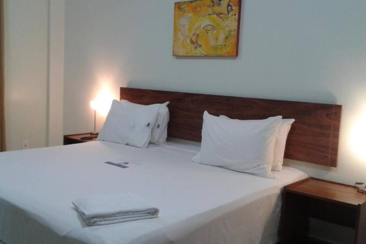 Quarto de hotel com uma cama grande, duas mesas de cabeceira e um quadro na parede.