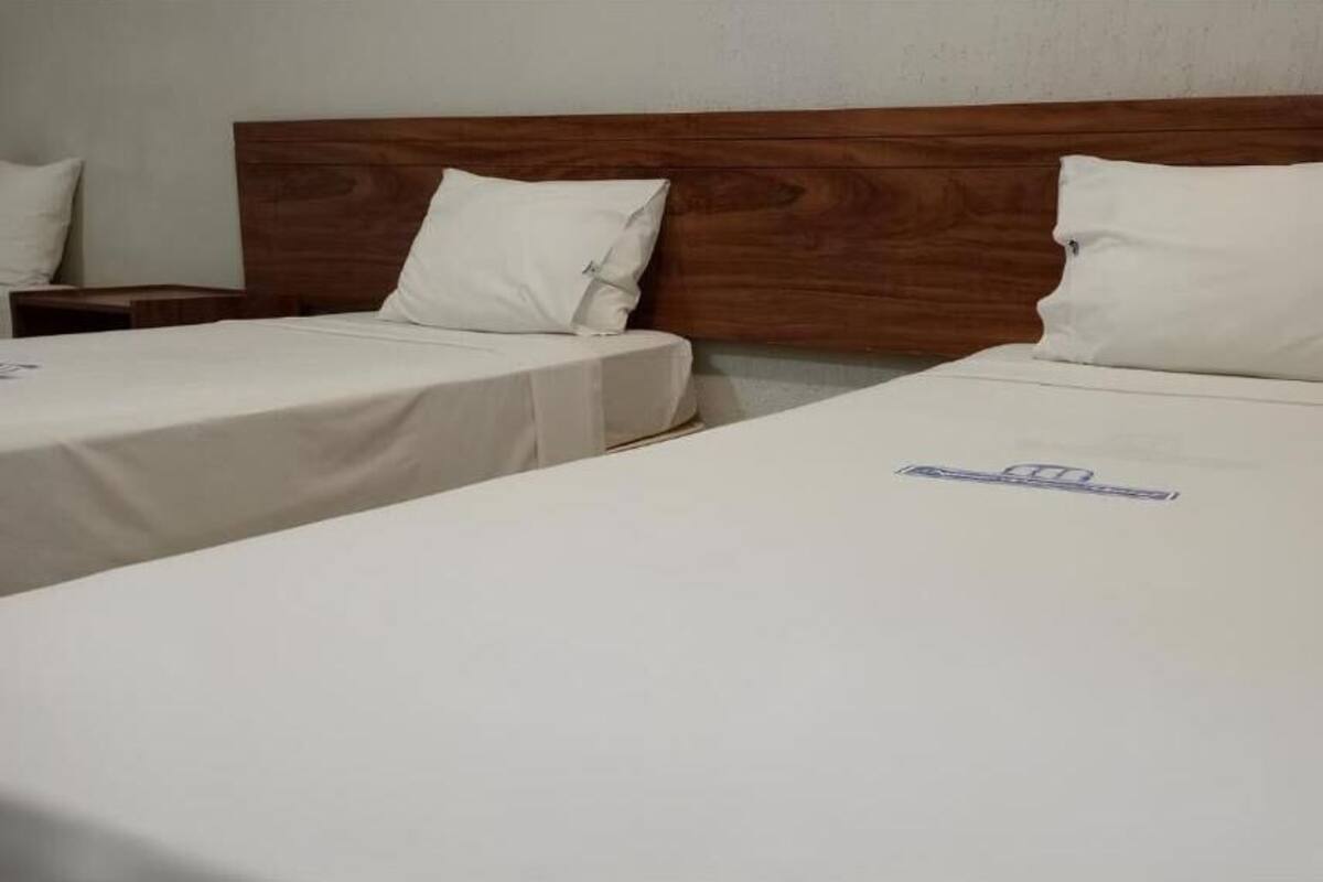 Quarto de hotel com duas camas de solteiro, cada uma com cabeceira de madeira e roupa de cama branca.