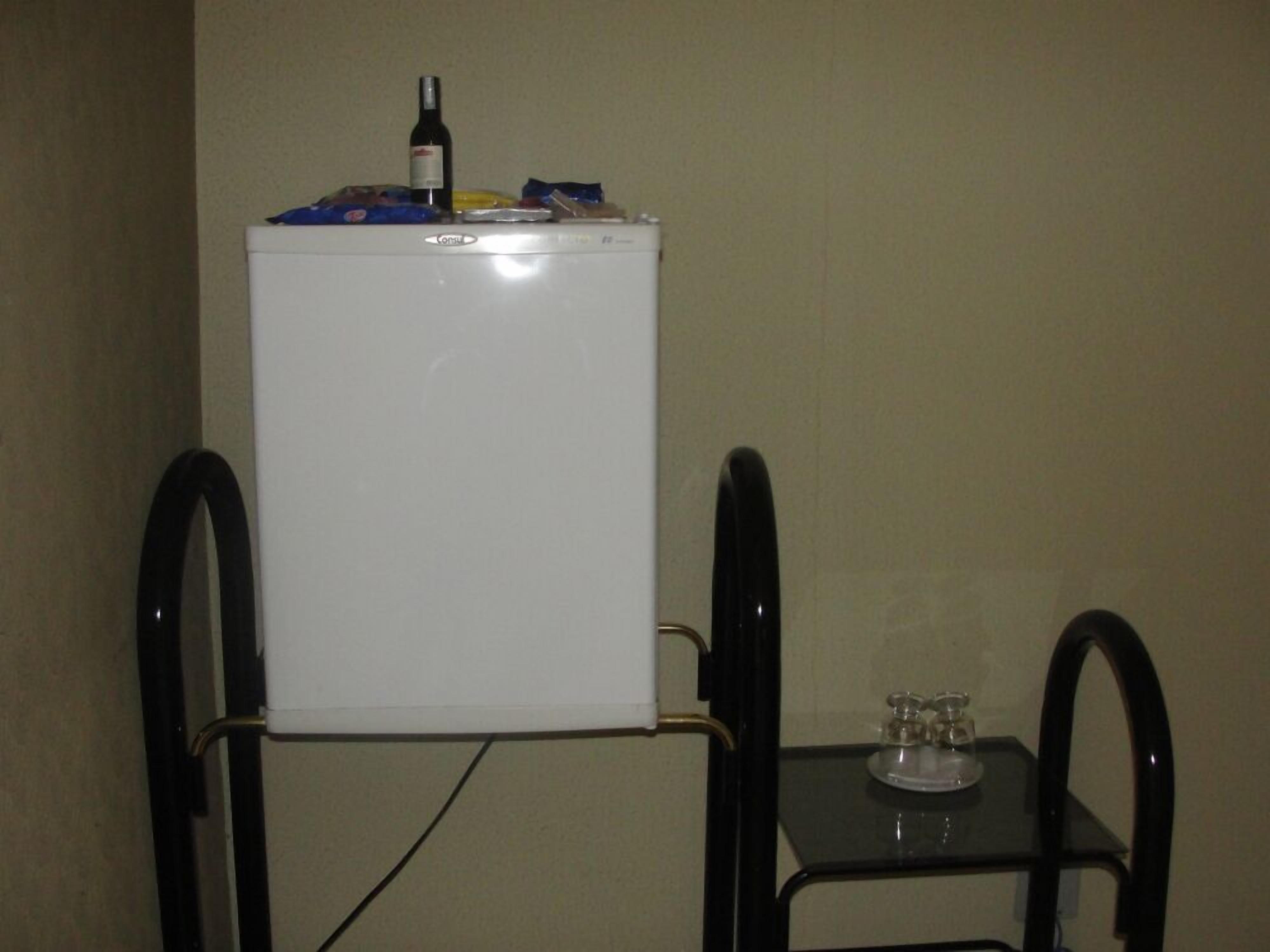 Uma pequena cozinha compacta com um refrigerador branco, uma mesa com duas cadeiras e uma garrafa de vinho sobre o refrigerador.