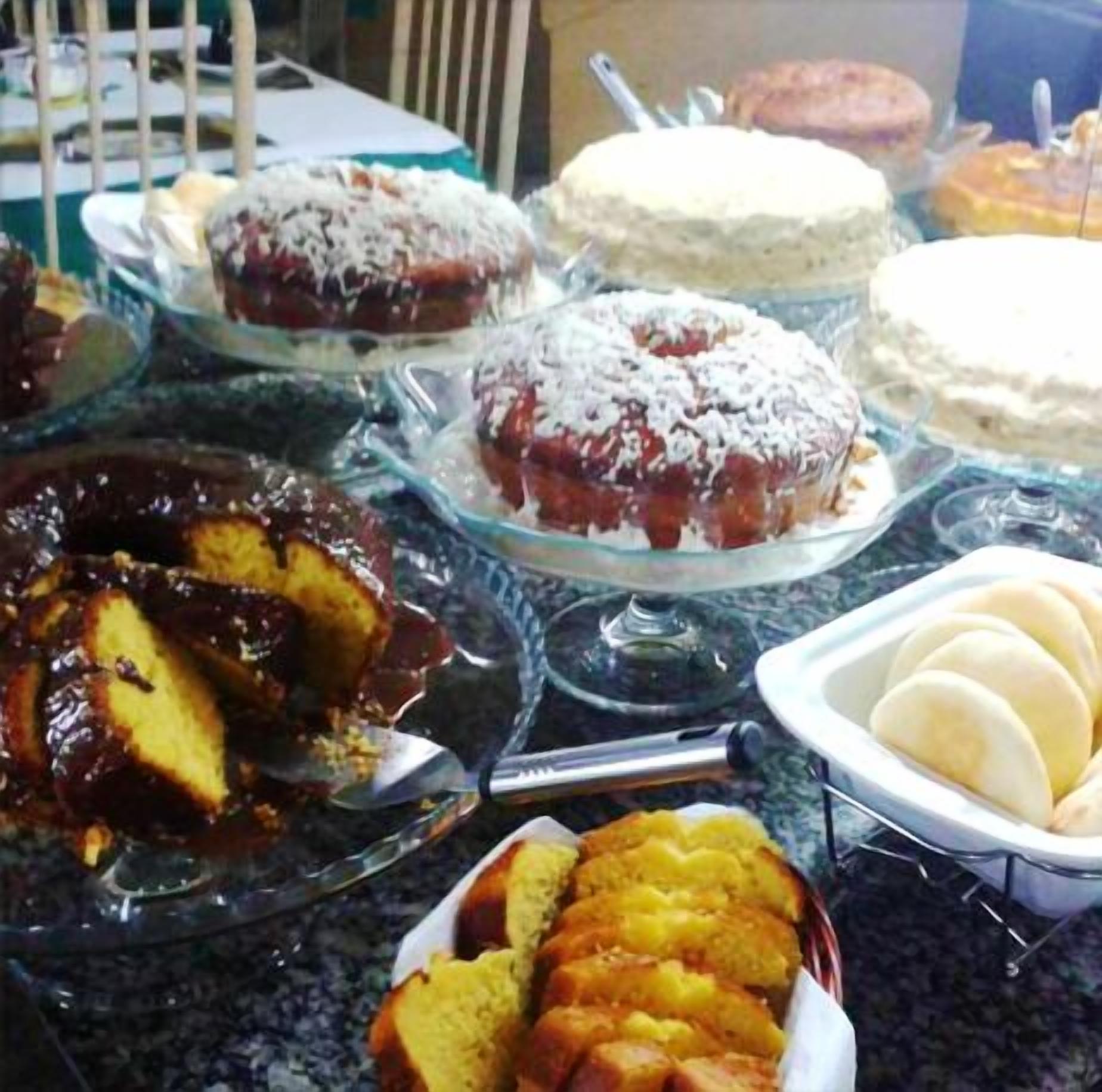 Diversas sobremesas expostas, incluindo bolos e doces, dispostas em travessas de vidro.