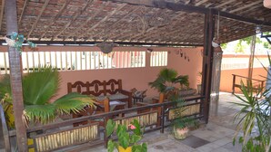 Uma área de varanda coberta com móveis de madeira, plantas em vasos e piso de azulejos.