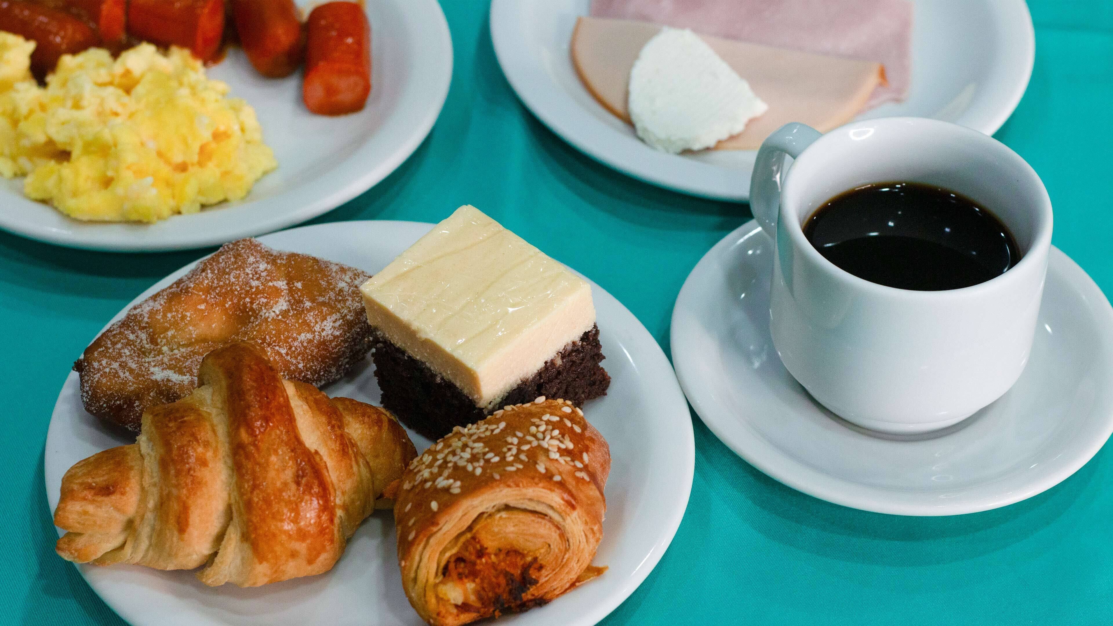 Uma mesa com pratos de comida, incluindo doces, um cheesecake e uma xícara de café.