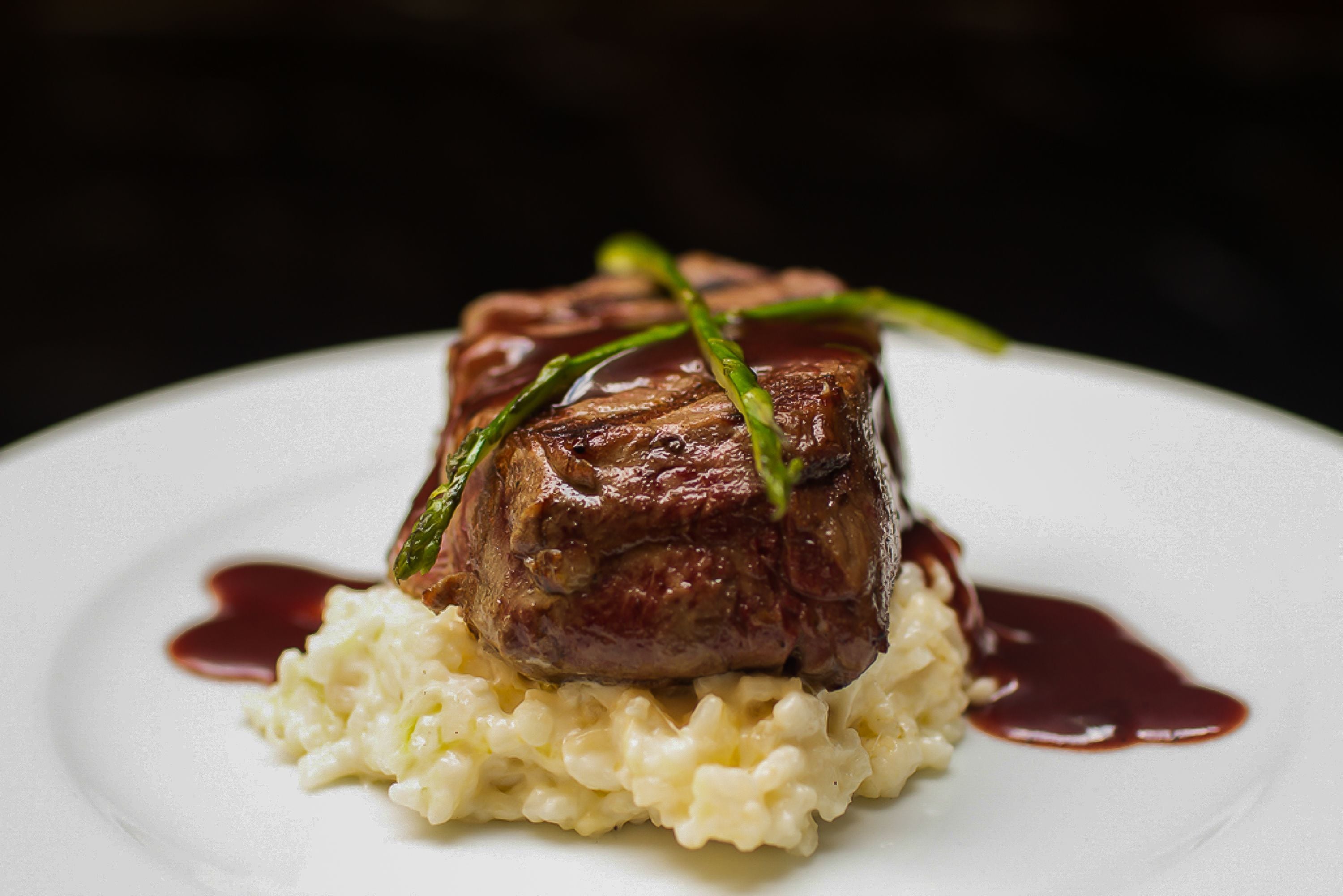 Um prato com carne, aspargos e molho cremoso.