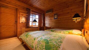 Quarto de cabana de madeira com duas camas, uma janela com cortinas e uma luminária fixada na parede.